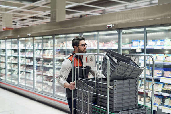 Sales clerk pushing cart with plastic crates at supermarket - Royalty ...