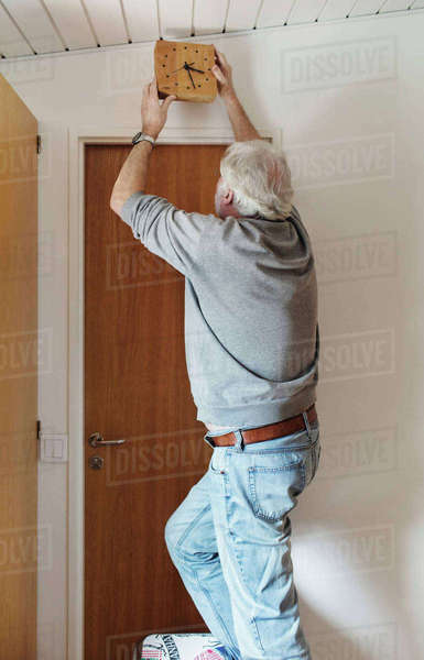 Senior man hanging wall clock above door at home - Stock Photo - Dissolve