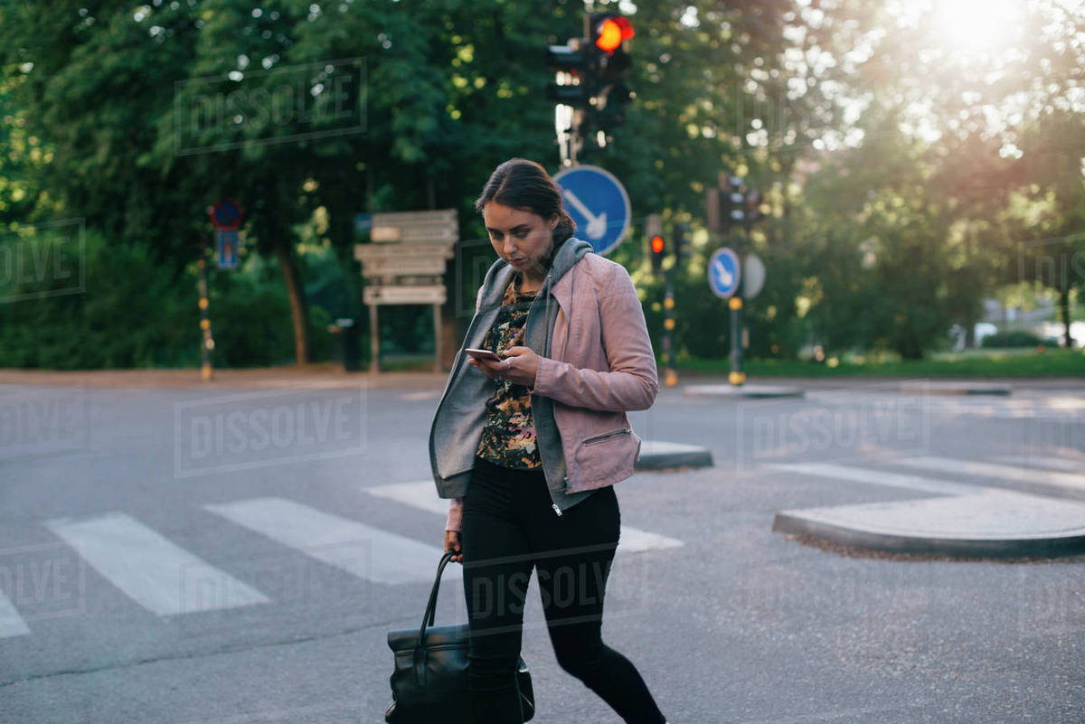 Young woman crossing street while using smart phone in city - Royalty ...
