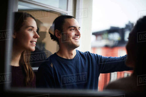 Smiling man with friends looking through window while standing in ...