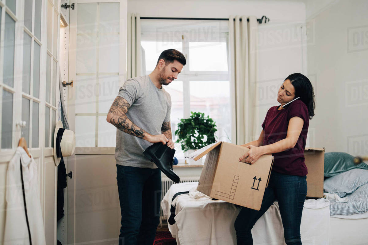 Man removing shoes from box while woman talking on phone at new home ...