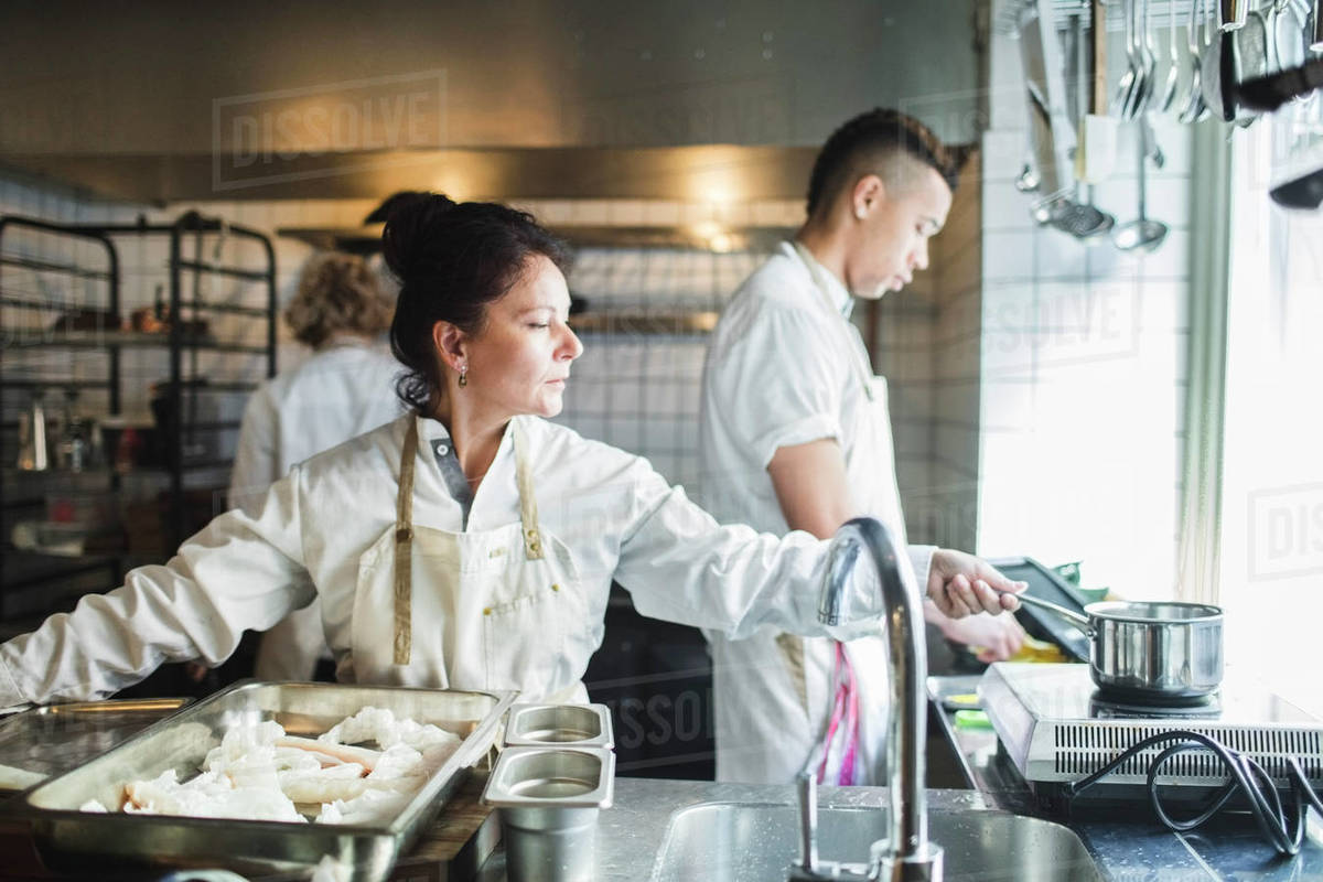 Mature female chef cooking on stove while working in kitchen against ...
