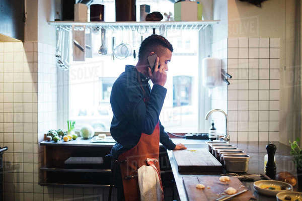 Side view of mature chef talking on mobile phone while standing at ...