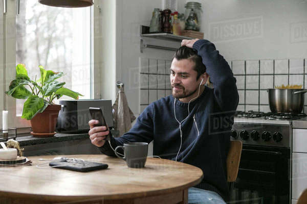 Man with headphones using mobile phone while sitting at table in ...