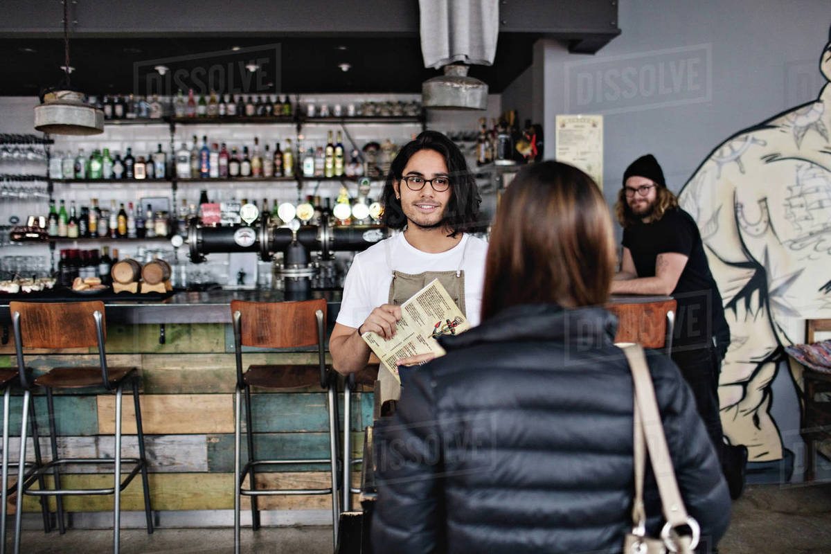 Waiter showing menu to female customer while standing at restaurant ...