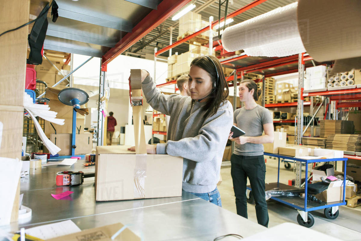 Woman packing box while coworkers discussing in distribution warehouse ...