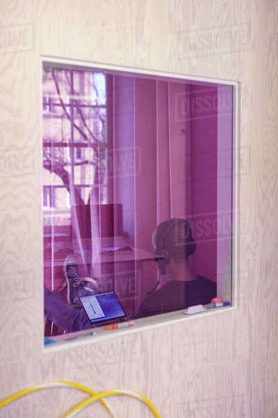 Creative businessman using laptop seen through window in office ...