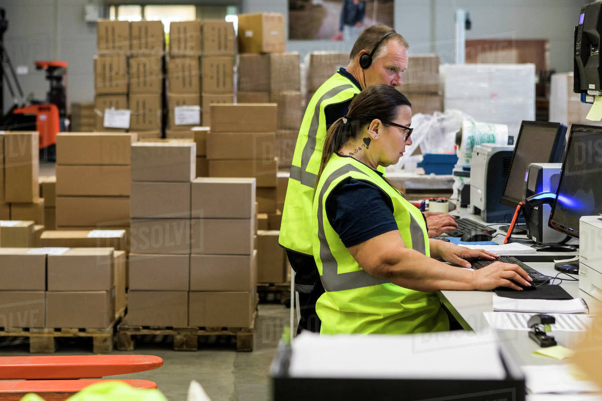 Side view of confident workers using computers at desk in distribution ...