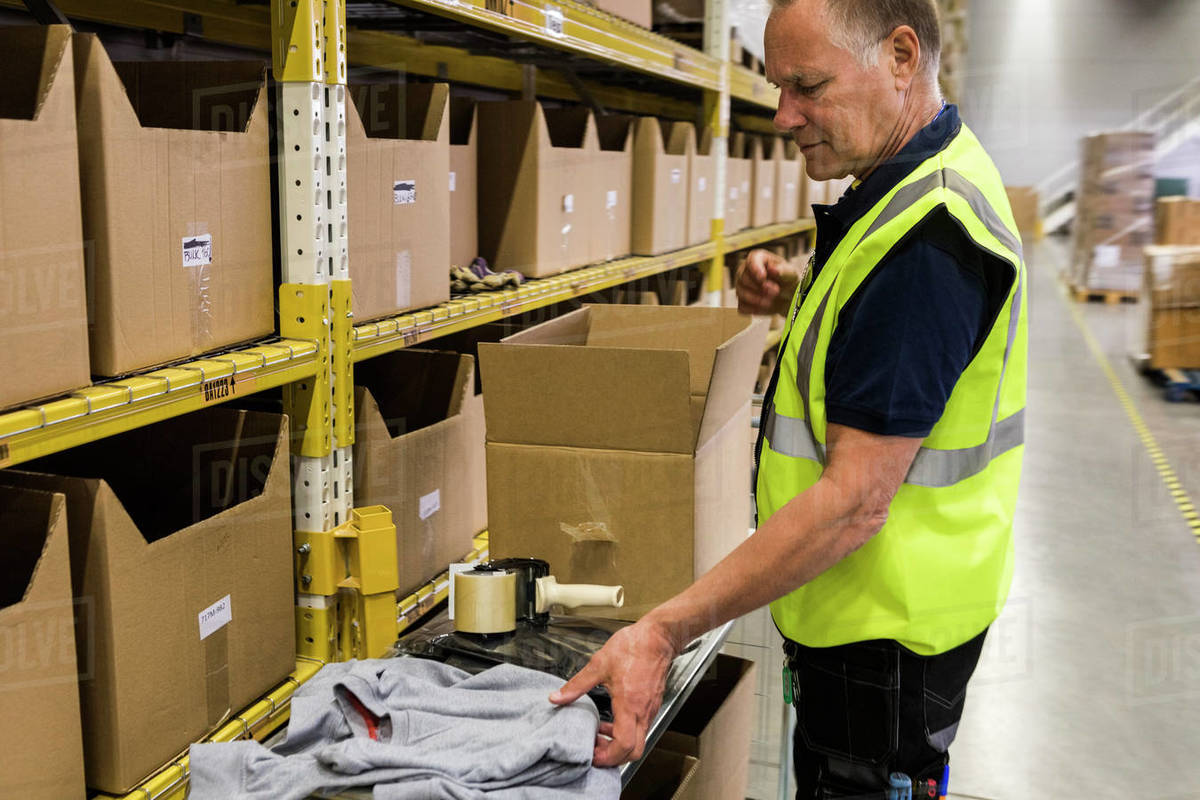 Side view of senior male worker packing merchandise in cardboard box at ...