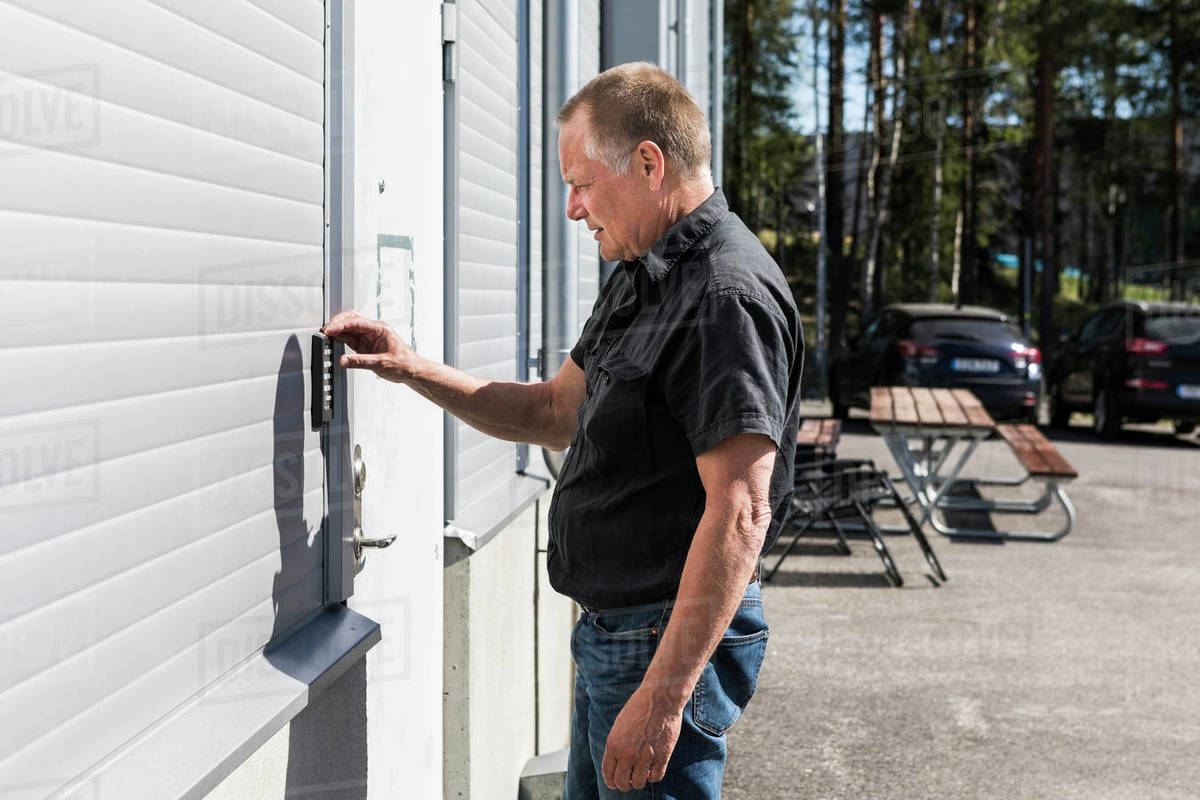 Side view of senior man unlocking door at warehouse entrance - Royalty ...