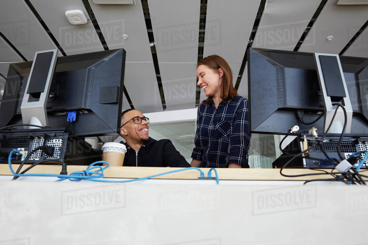 Low angle view of smiling friends talking while using computers at ...