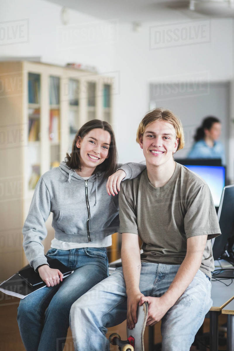 Portrait of smiling high school students sitting on desk in computer ...