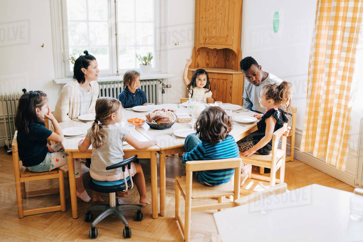 Teachers and students sitting at table during lunch break in classroom ...