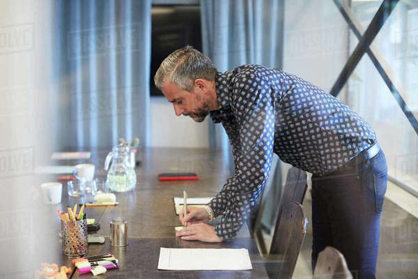 Side view of mature businessman writing on paper while standing at ...