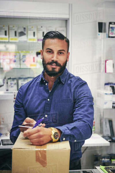 Portrait of salesman writing on box while holding mobile phone in ...