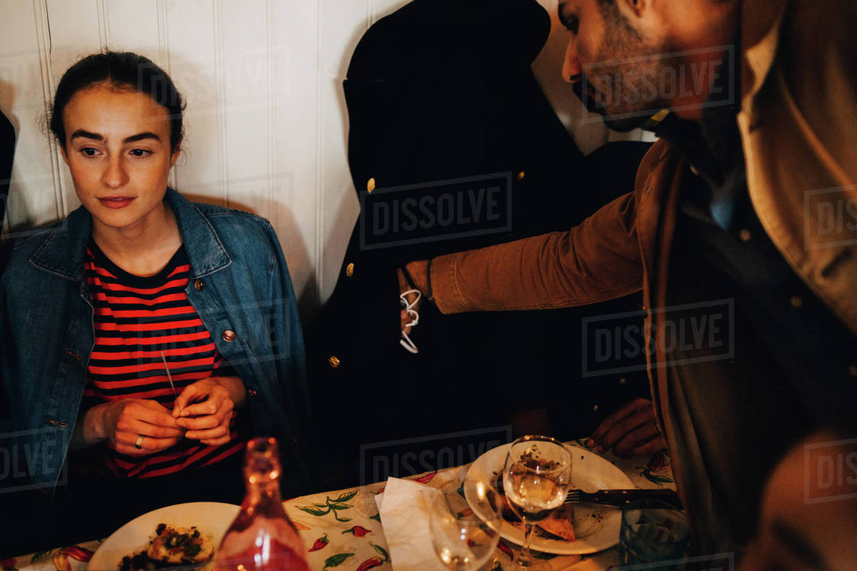 Young man putting hand in jacket's pocket by woman sitting in ...