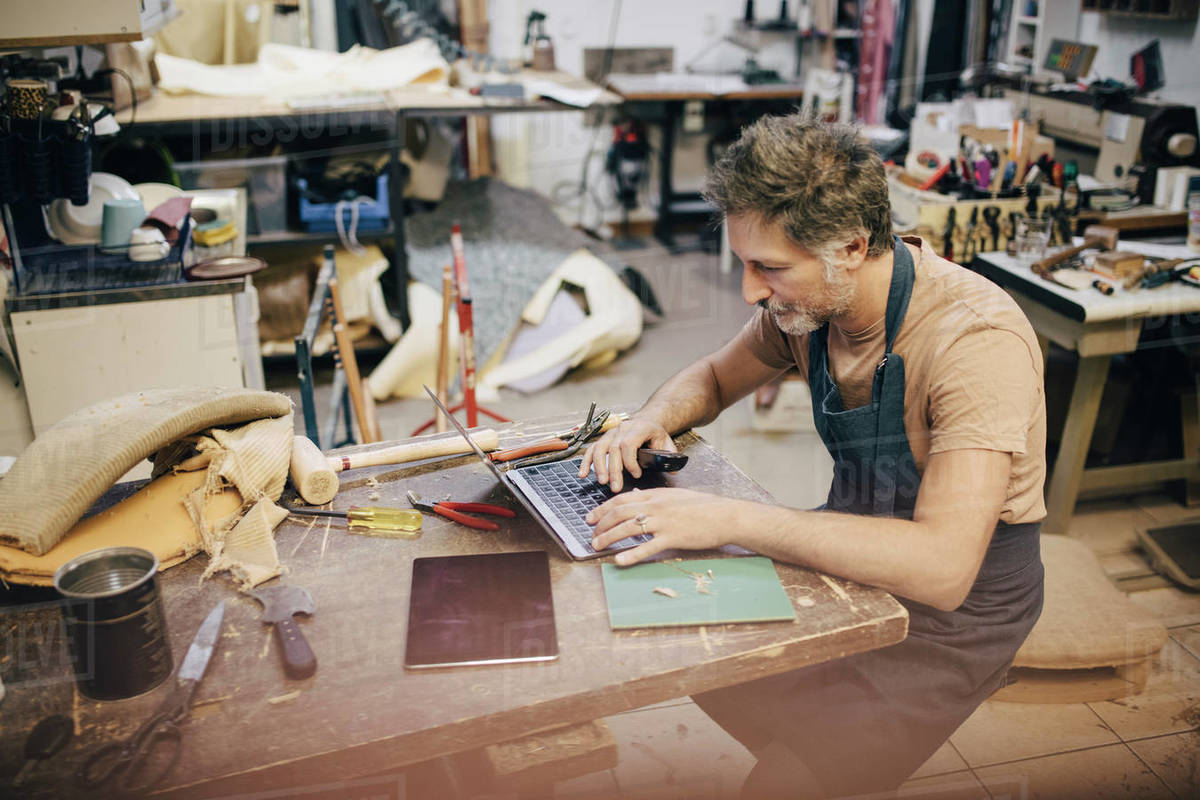 Male craftsperson using laptop at workbench in workshop - Royalty-free ...
