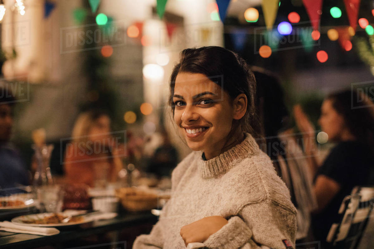 Portrait of smiling young woman sitting at table during dinner party in ...