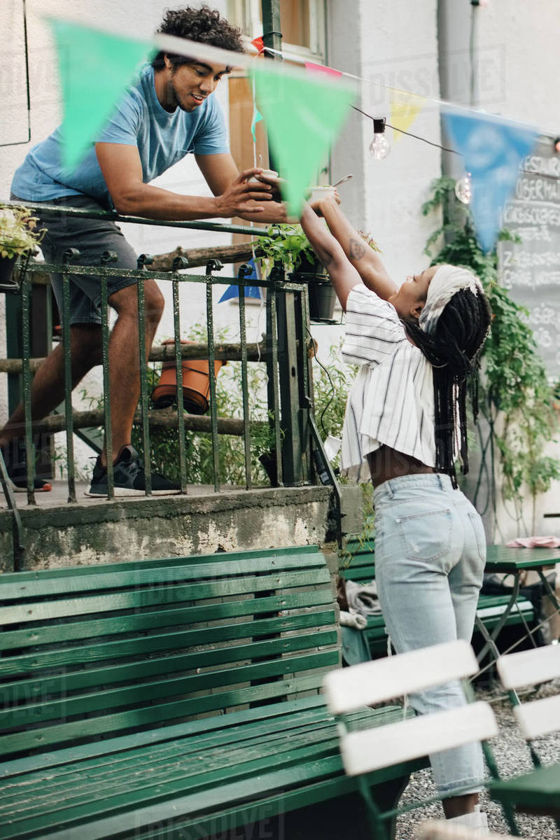 Young man giving food to female friend from balcony during garden party ...