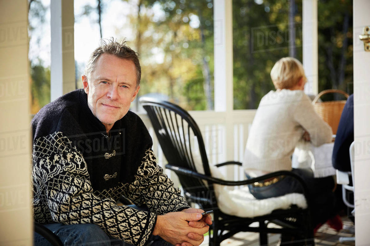 Portrait of smiling mature man sitting on porch with friend sitting in ...