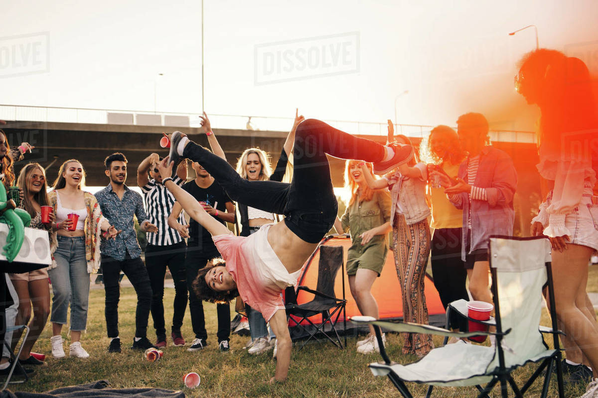 Happy friends looking at man dancing in musical event against sky in ...