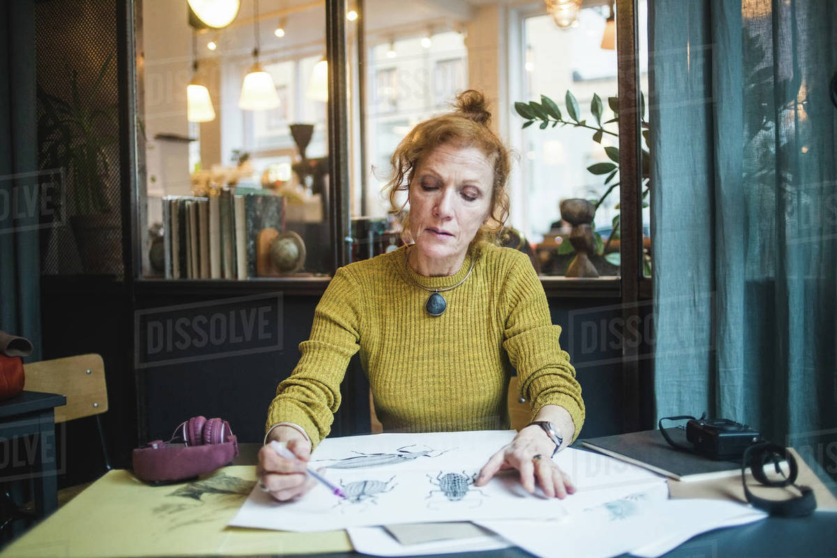 Confident mature female illustrator drawing on paper at desk in ...