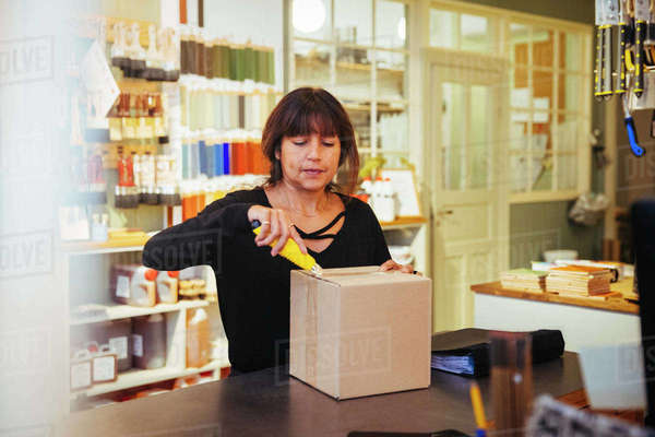 Mature female owner opening cardboard box at checkout counter in ...