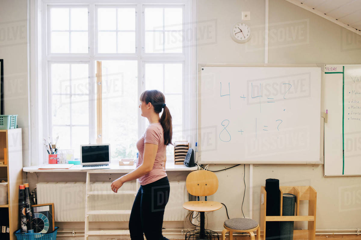 Side view of teacher walking by whiteboard with mathematics in ...