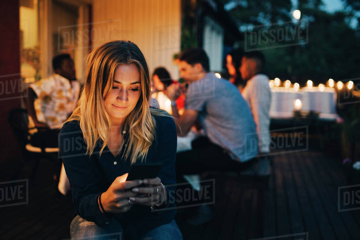 Young woman using smart phone while friends in background during dinner ...