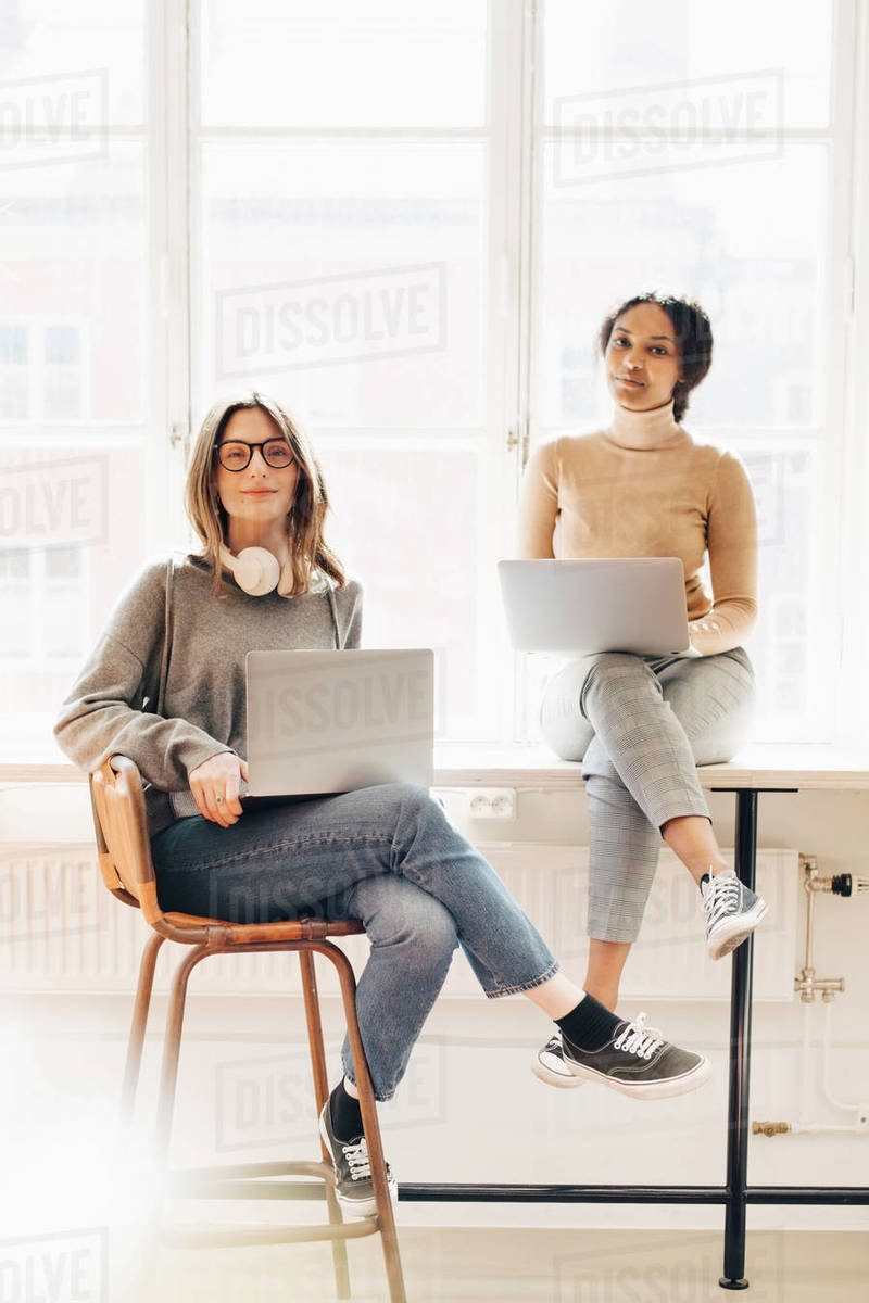 Portrait of female computer programmers with laptops sitting at desk in ...