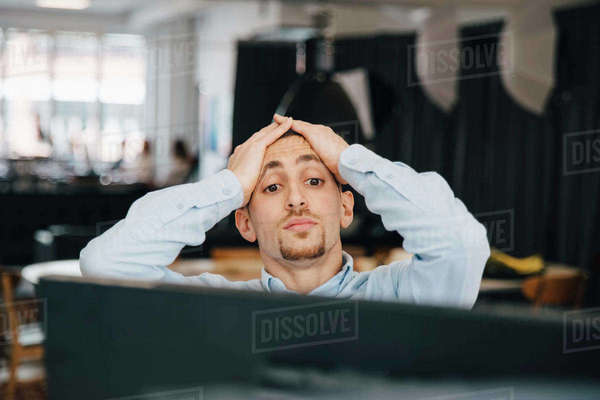 Exhausted computer programmer with head in hands looking at computer ...