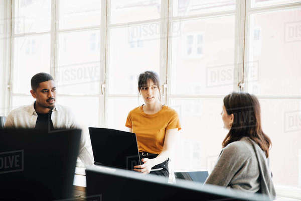 Female software engineer explaining to coworkers while sitting against ...