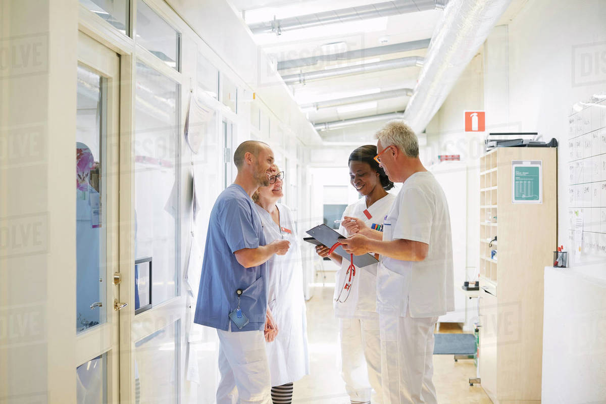 Smiling healthcare workers discussing while standing in corridor at ...