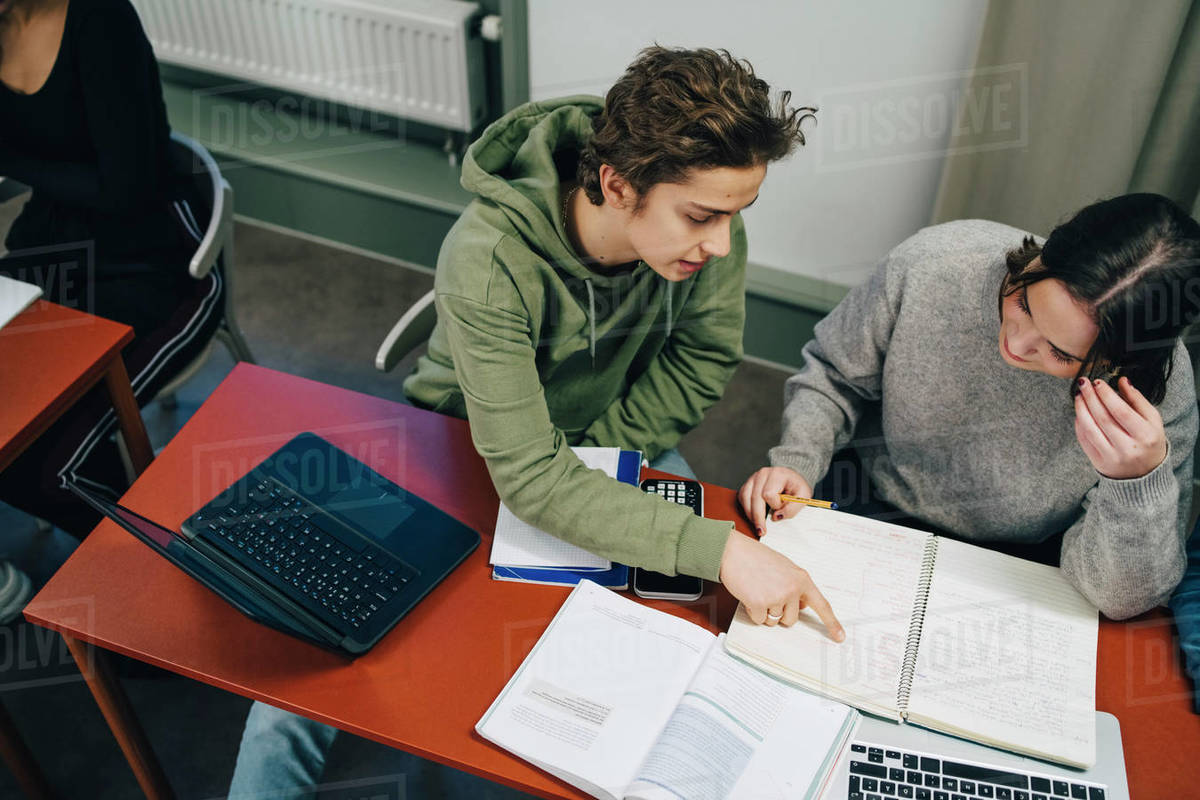 High angle view male student assisting female classmate at desk in ...