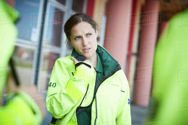 Female paramedic looking away while talking on walkie-talkie outside ...