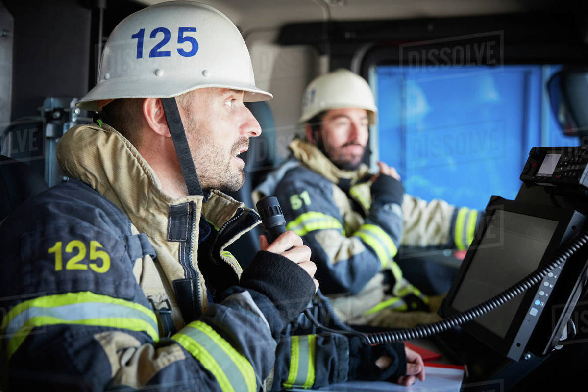 Firefighter talking on microphone while sitting with coworker in fire ...