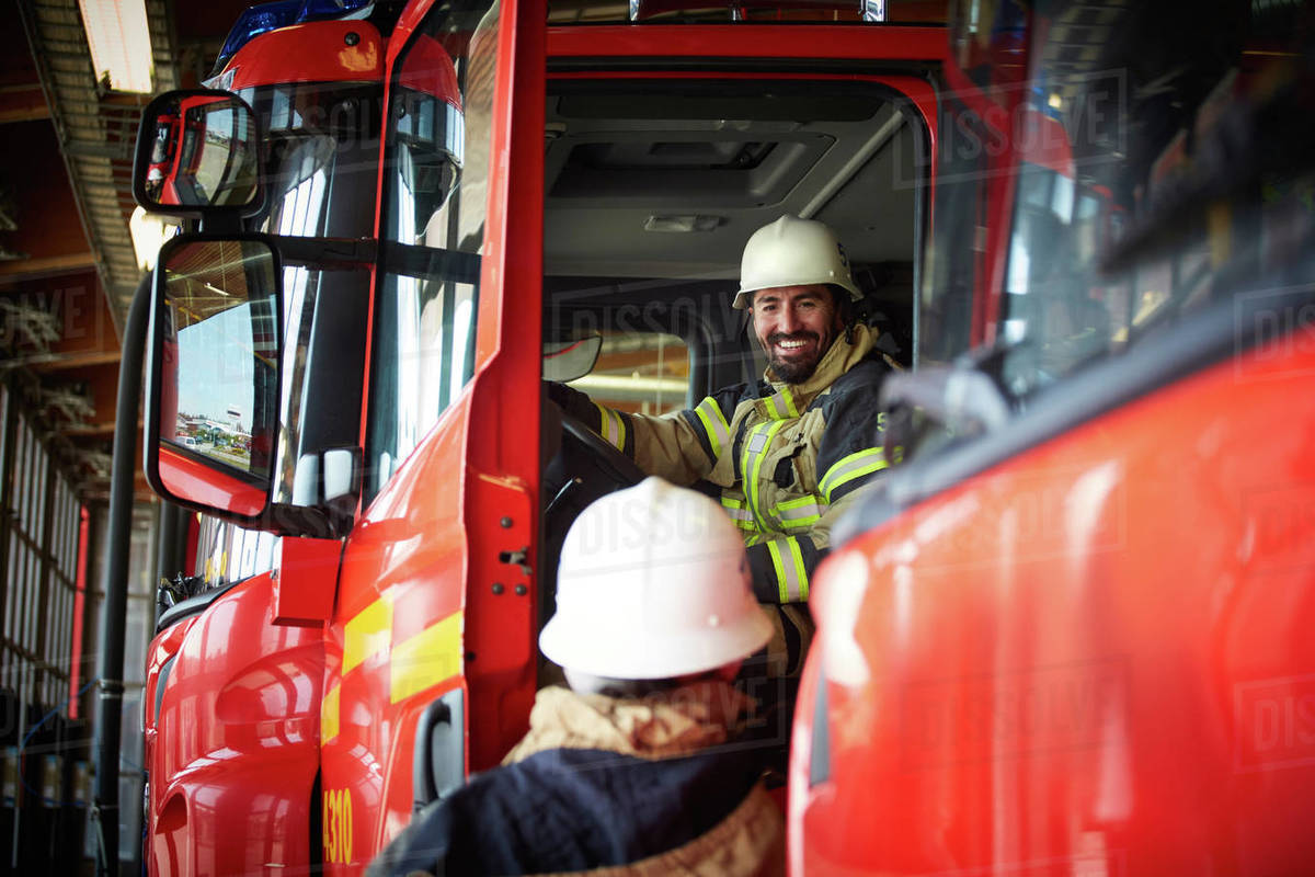 Smiling firefighter talking to coworker while sitting in fire truck at ...