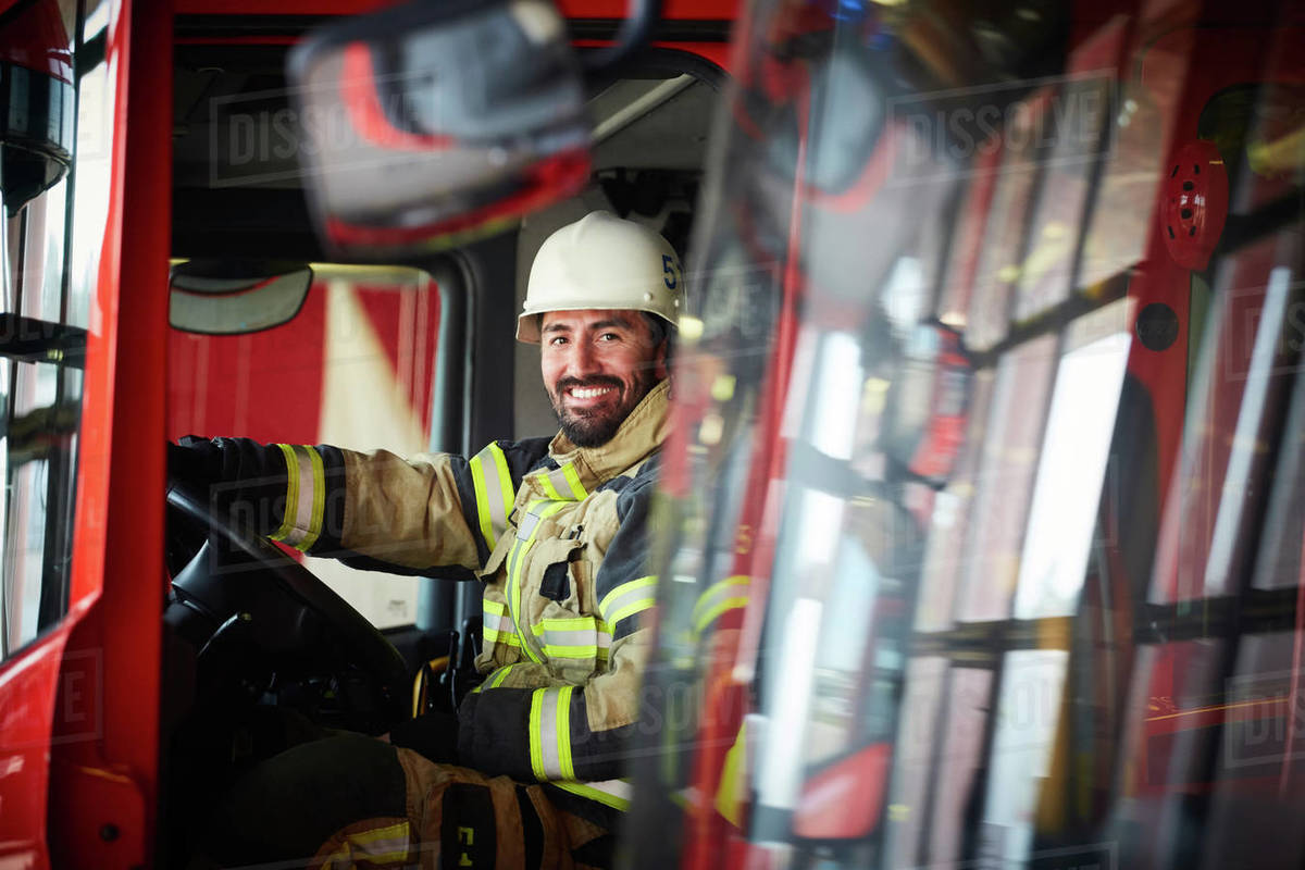 Portrait of mid adult firefighter sitting in fire truck at fire station ...