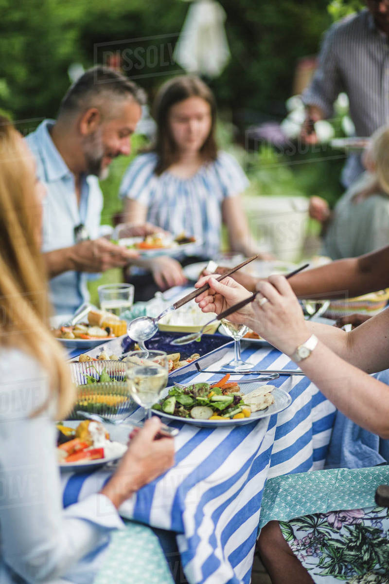 Woman serving food while sitting with friends and family at backyard ...