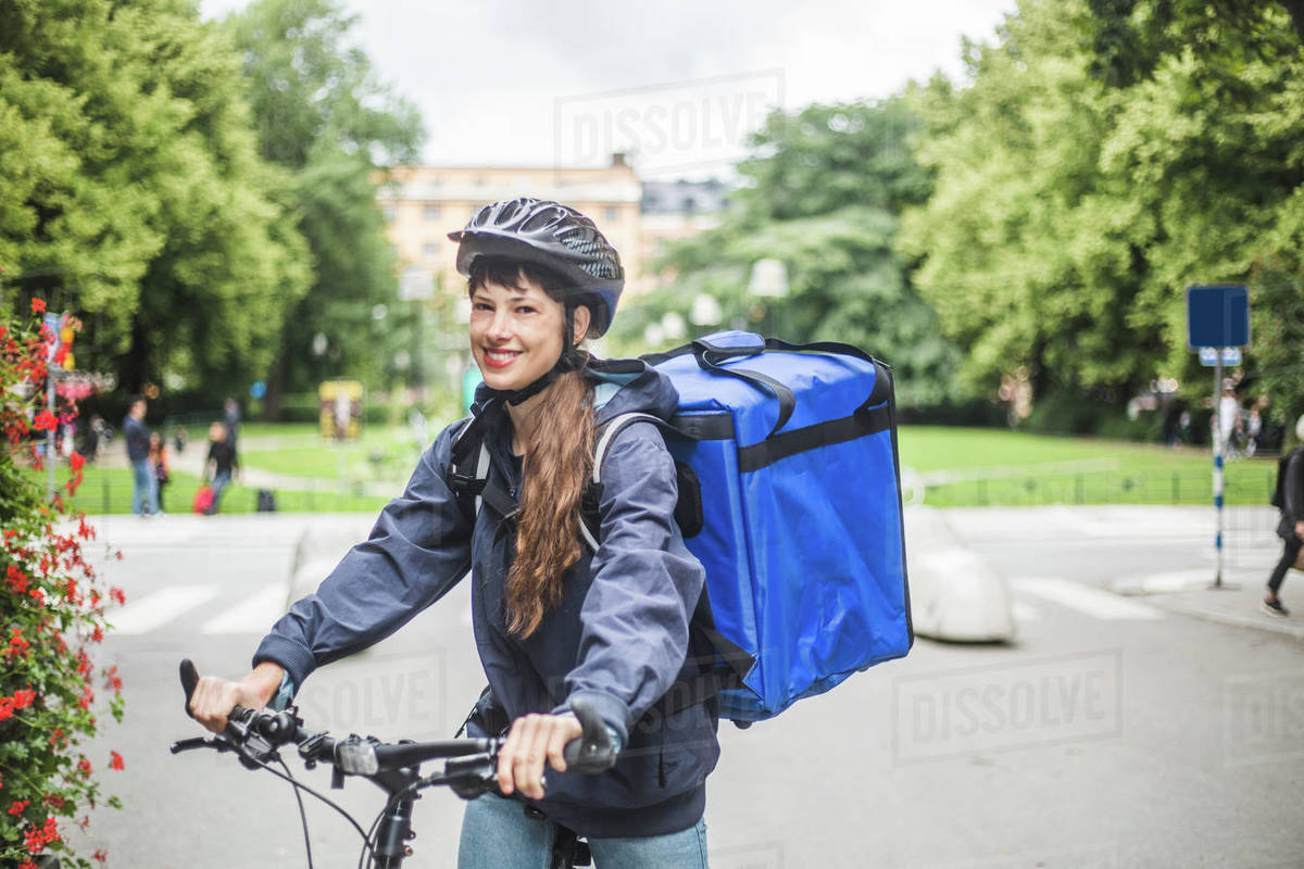 Portrait of smiling food delivery woman with bicycle on street in city ...