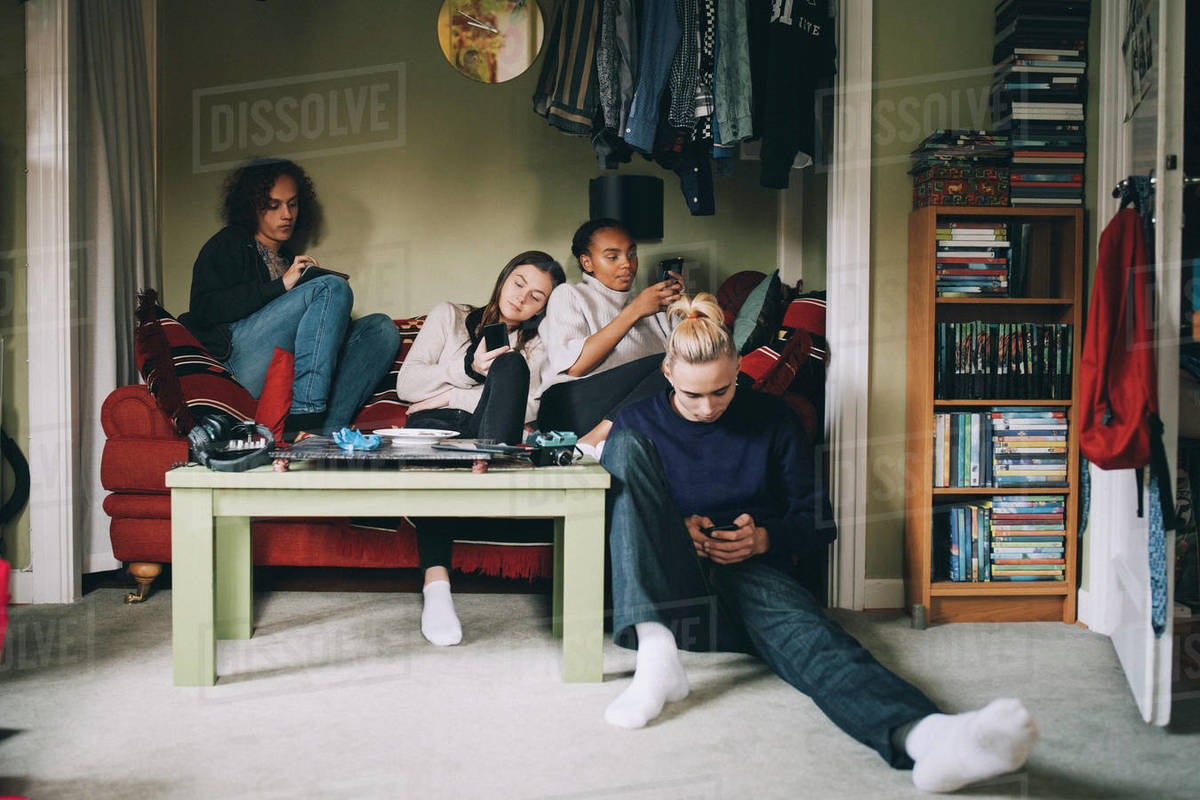 Distracted friends using smart phones while sitting together at home ...