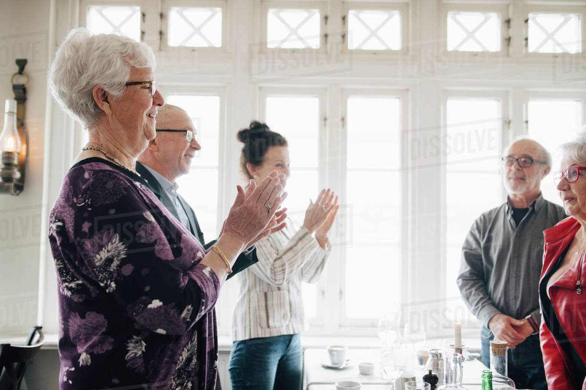 Male and female friends clapping hands while standing by table in ...