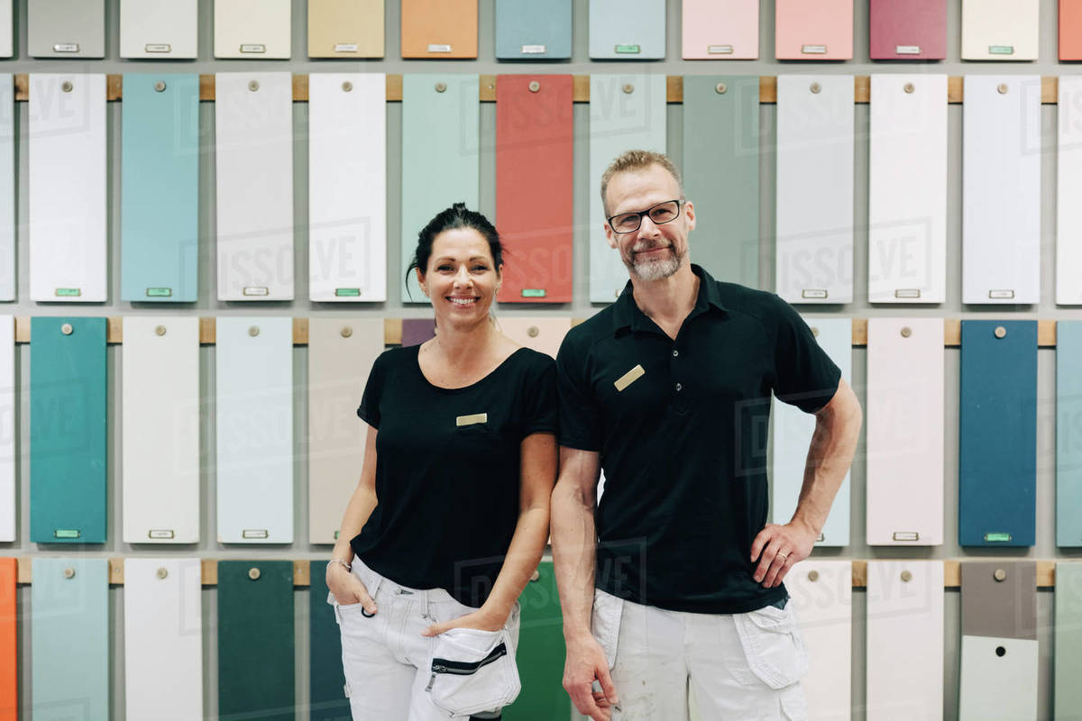 Portrait of smiling sales employees standing against multi colored wall ...
