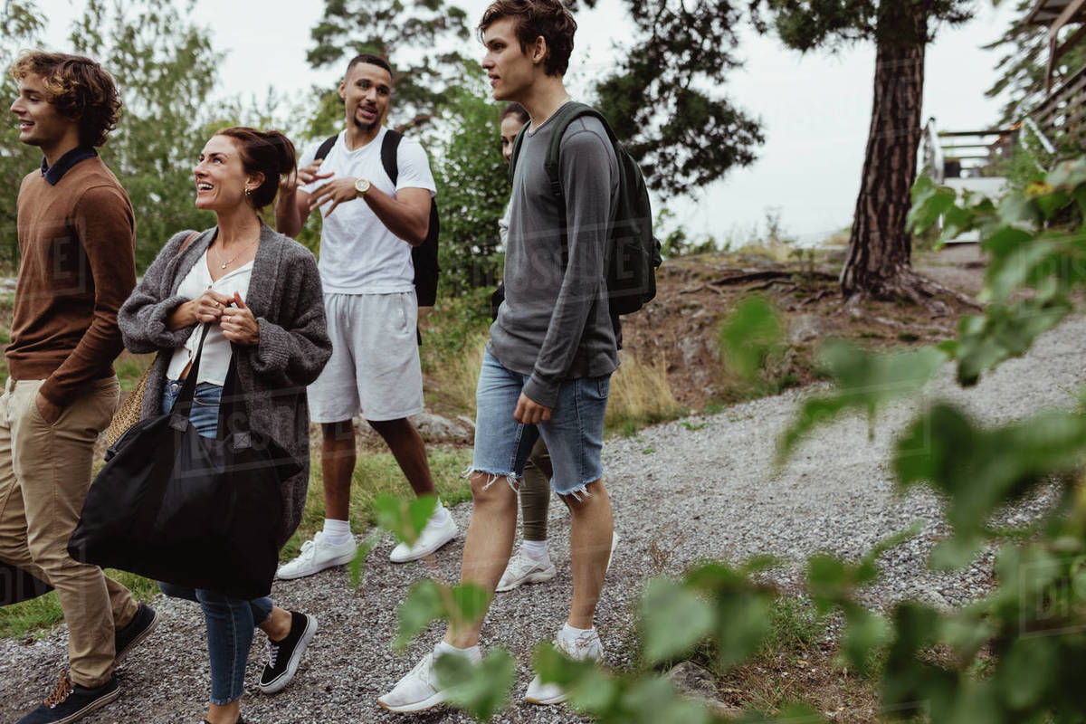 Smiling friends and family walking on footpath amidst trees during ...