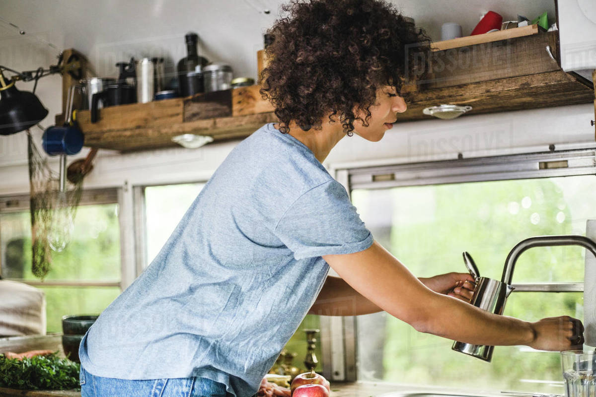 Side view of Afro woman filling kettle from faucet in motor home ...
