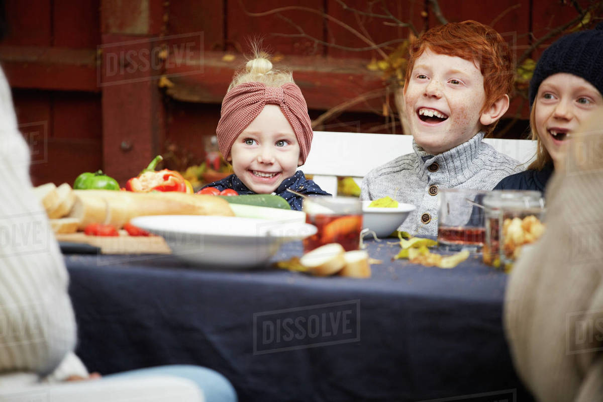 Happy male and female siblings sitting by table for meal - Royalty-free ...