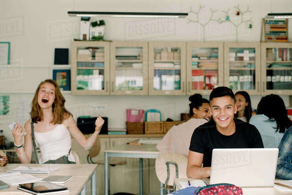 Portrait of male students using laptop while smiling female teenagers ...