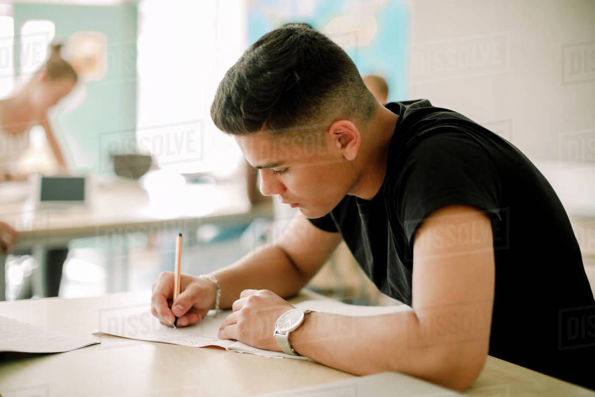 Teenage boy studying while sitting by table in classroom - Royalty-free ...