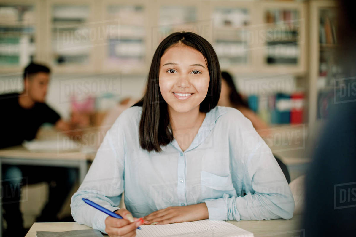 Portrait of smiling teenage girl studying at table in classroom - Stock ...