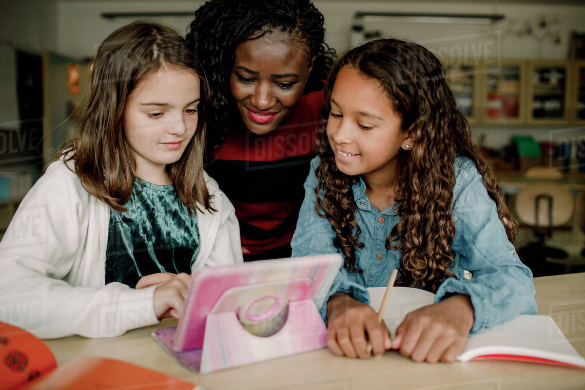 Female tutor with students looking at digital tablet in classroom ...